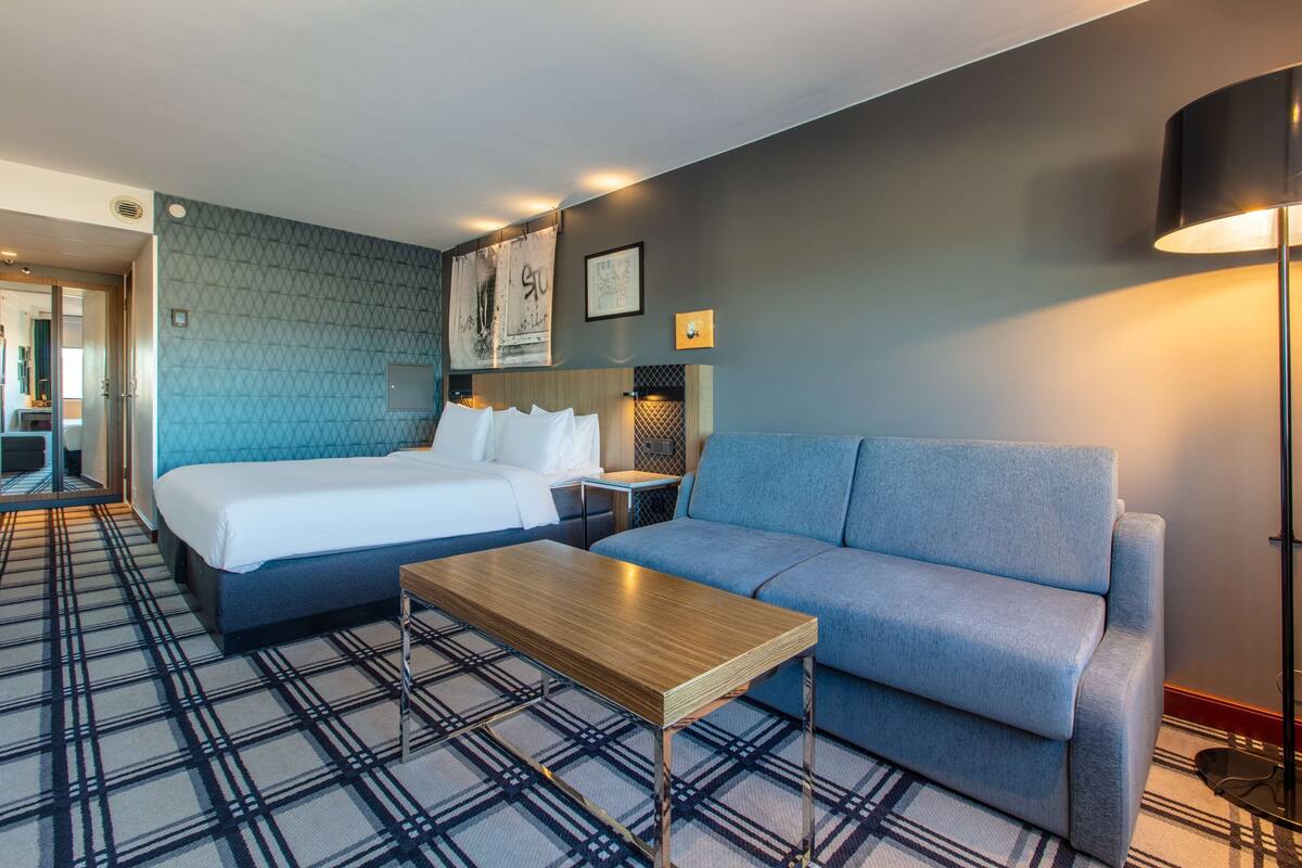 Quarto de hotel com cama, sofá, mesa de centro e abajur.