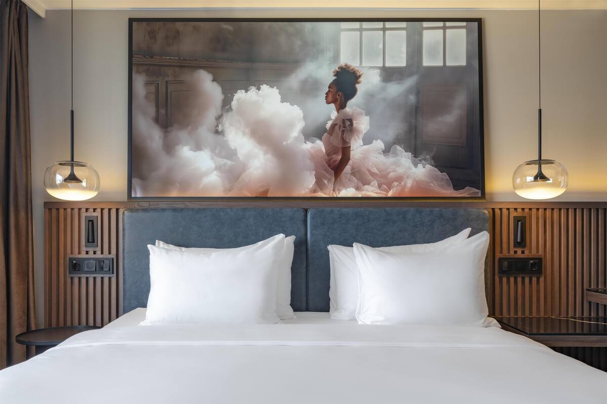 Uma cama com almofadas brancas, uma cabeceira azul e um quadro grande acima.
