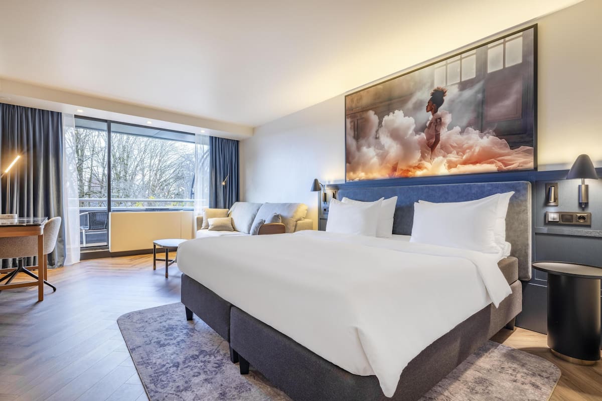 Quarto de hotel moderno com uma cama grande, uma escrivaninha, uma cadeira e vista para o exterior.