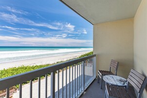 Uma varanda com vista para a praia, uma mesa e duas cadeiras.