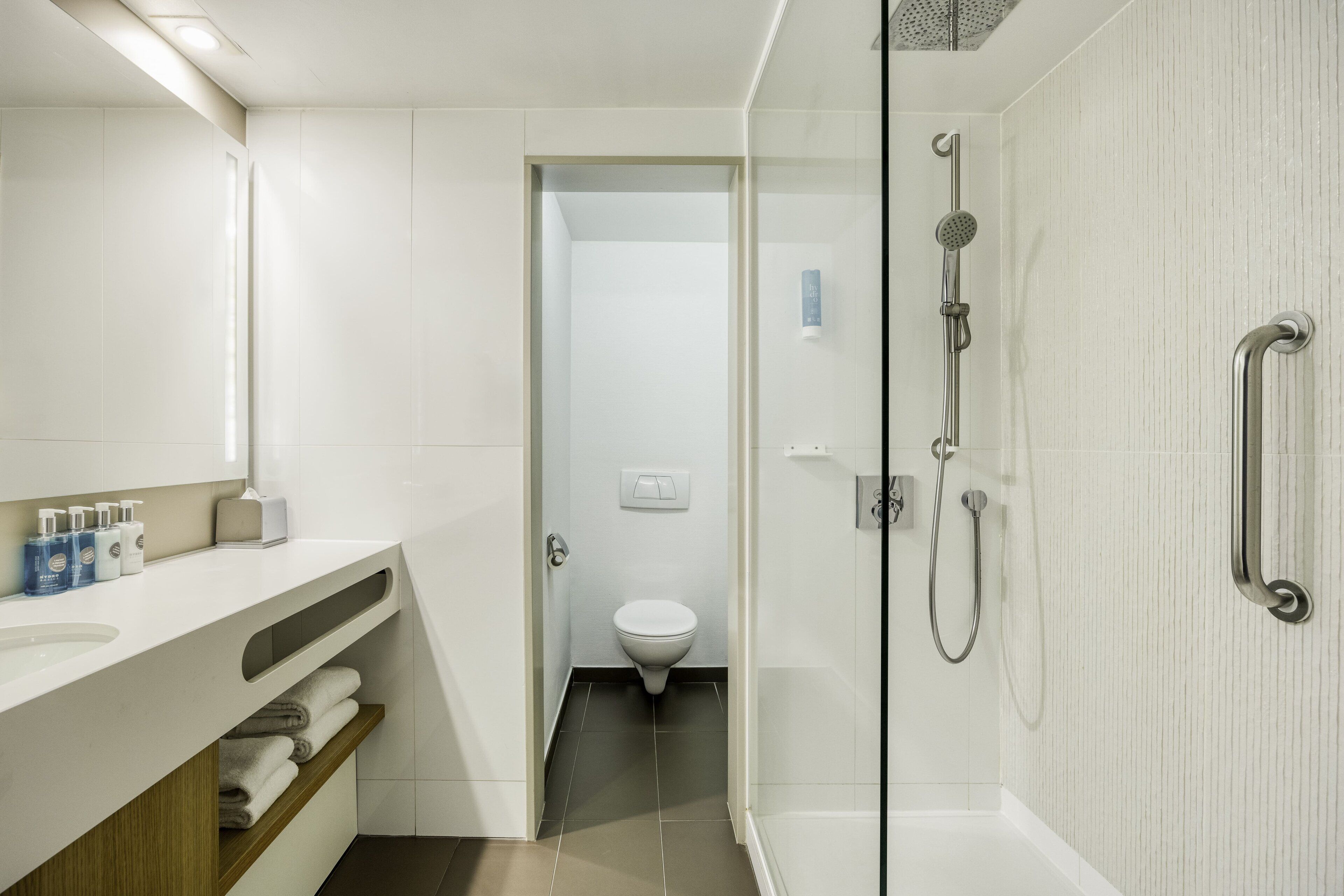 Casa de banho moderna com cabine de duche em vidro, sanita branca e espelho com produtos de higiene pessoal.