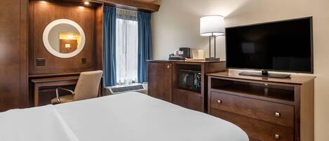 Quarto de hotel com uma cama grande, uma escrivaninha com lâmpada, televisão de tela plana e micro-ondas.