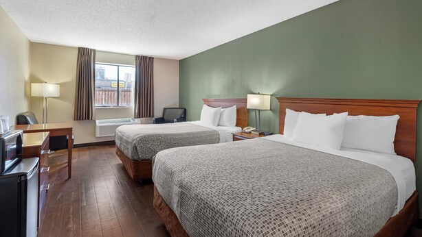 Quarto de hotel com duas camas, uma escrivaninha, uma cadeira, televisão e janela com cortinas.