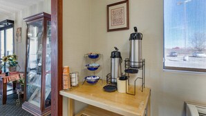 Quarto com mesa de madeira, cafeteira, quadro emoldurado e janela com vista para um parque de estacionamento.