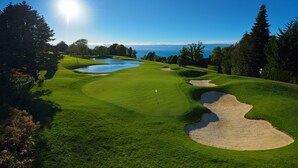 Um campo de golfe com haste de sinalização, bunkers de areia e lago.