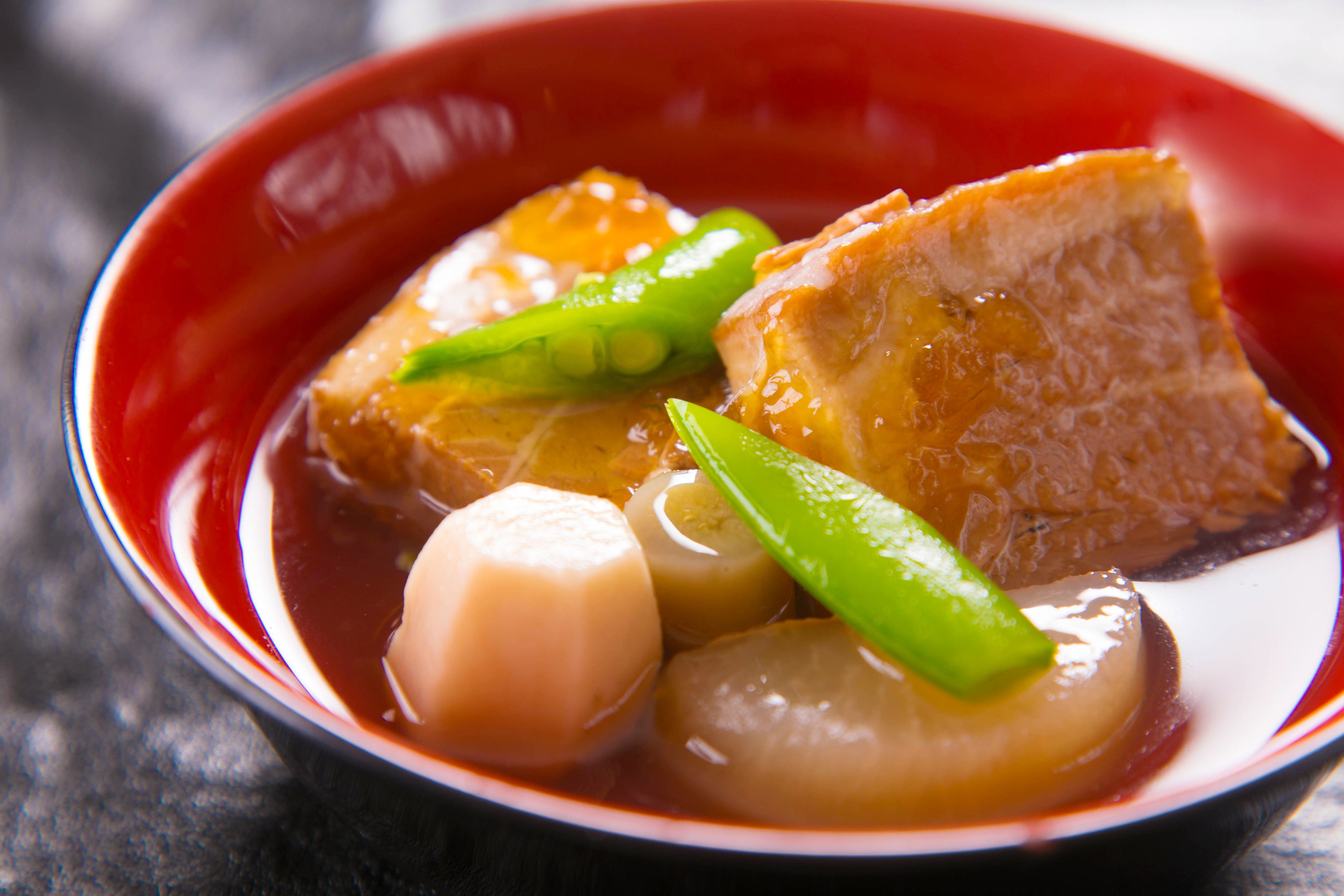 Uma tigela de sopa com tofu, vegetais verdes e uma fatia de carne.