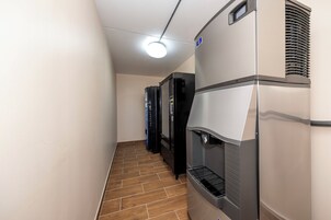 Um corredor com piso de azulejos, iluminação no teto e máquinas de venda automática.