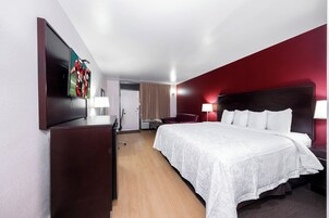 Quarto de hotel com uma cama grande, uma escrivaninha, uma cadeira, uma televisão e uma porta.