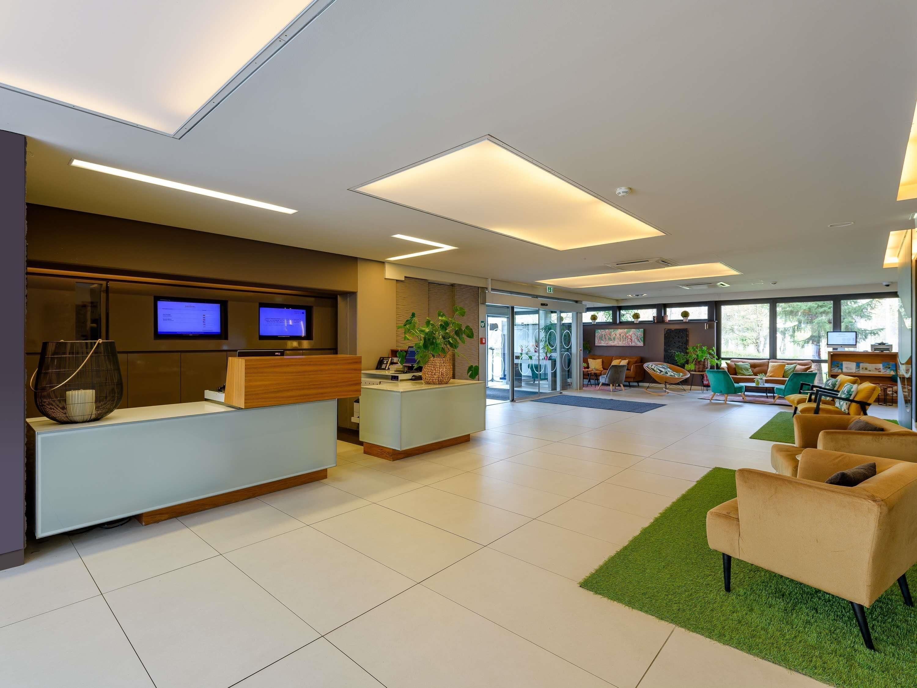 Uma área de recepção moderna, com balcão, dois monitores e um espaço de estar com sofás e mesa de centro.