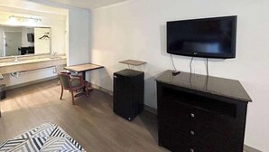 Quarto com um espelho grande, televisão de tela plana na parede, uma mesinha de madeira, um rack de entretenimento em tom escuro e um tapete estampado no chão.