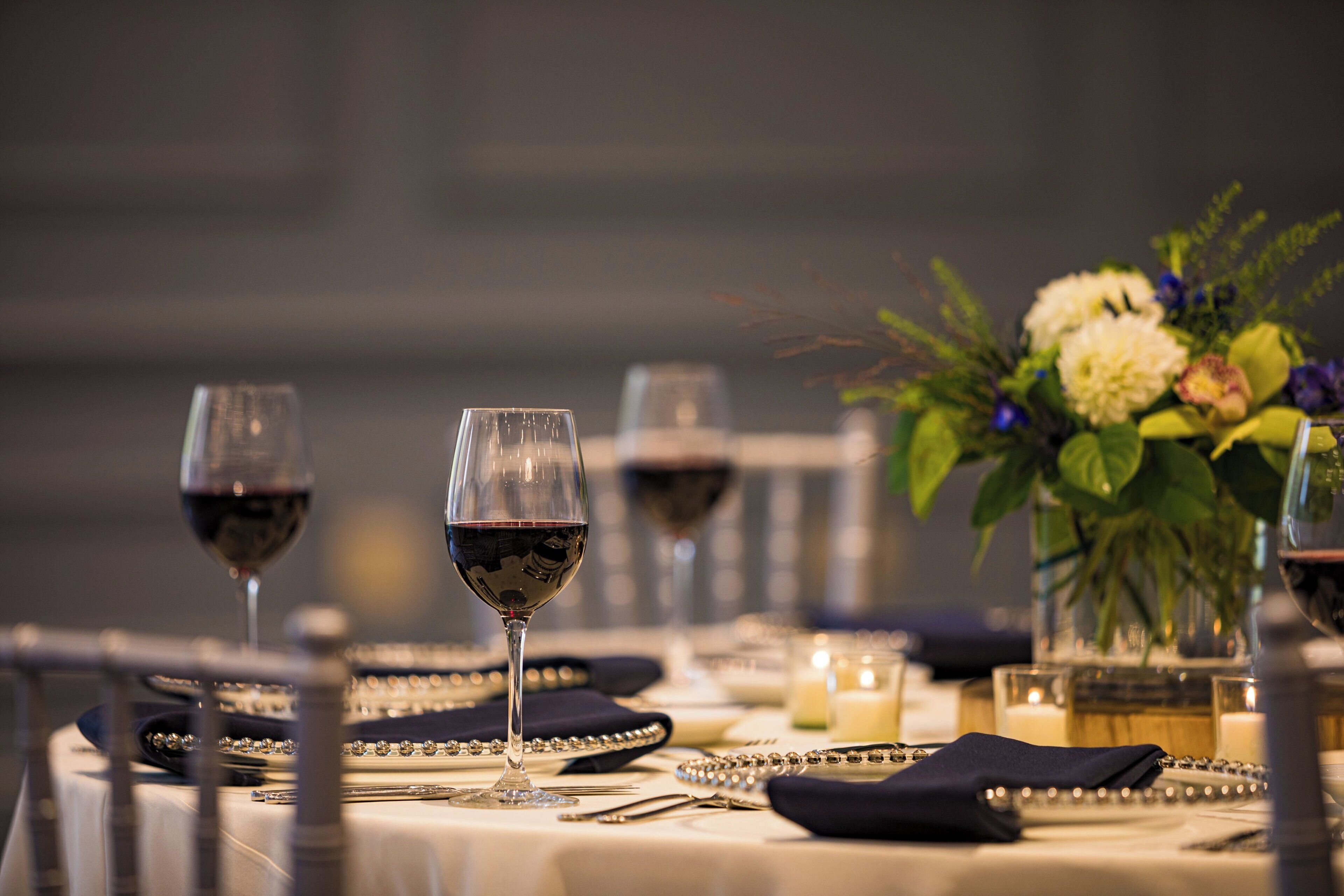 Mesa posta com taças de vinho, pratos e um arranjo floral no centro.