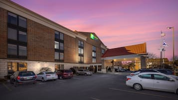 Um hotel com fachada de tijolos, telhado vermelho e estacionamento com vários carros.