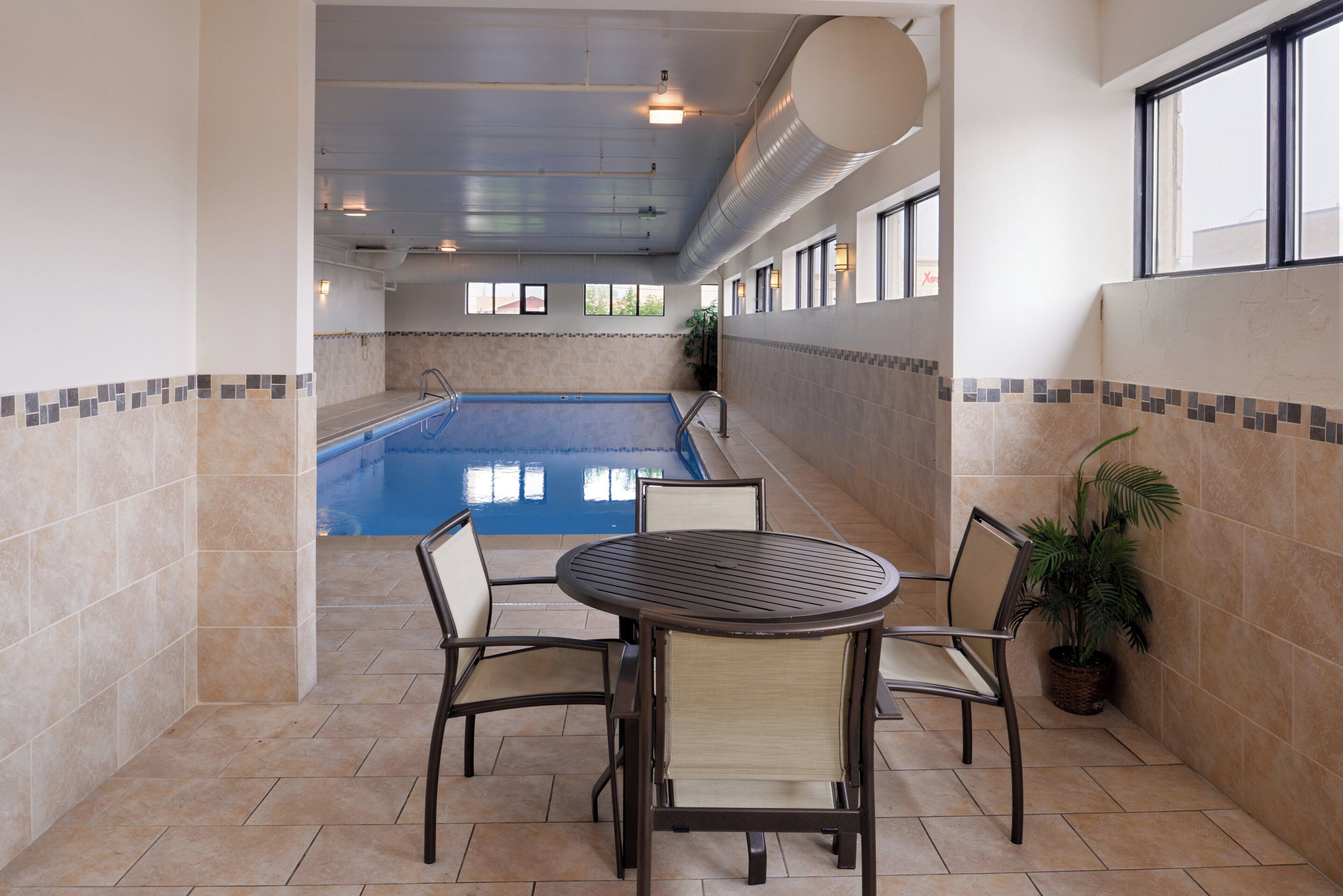 Área interna da piscina com vista para a piscina, uma mesa com cadeiras e um vaso de planta.