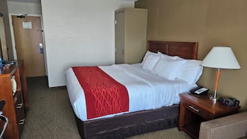Quarto de hotel com cama, escrivaninha, cadeira, abajur e telefone.