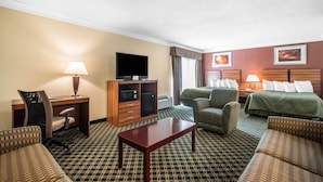 Quarto de hotel com cama, duas poltronas, escrivaninha com abajur, televisão e minibar.