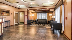 Um saguão de hotel com balcão de recepção, um sofá, cadeiras, um tapete estampado e um teto com claraboias.