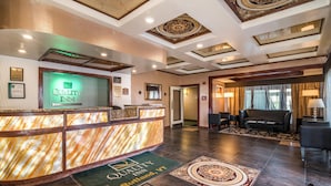 Um saguão de hotel com balcão de recepção, área de estar com um piano e teto decorativo.