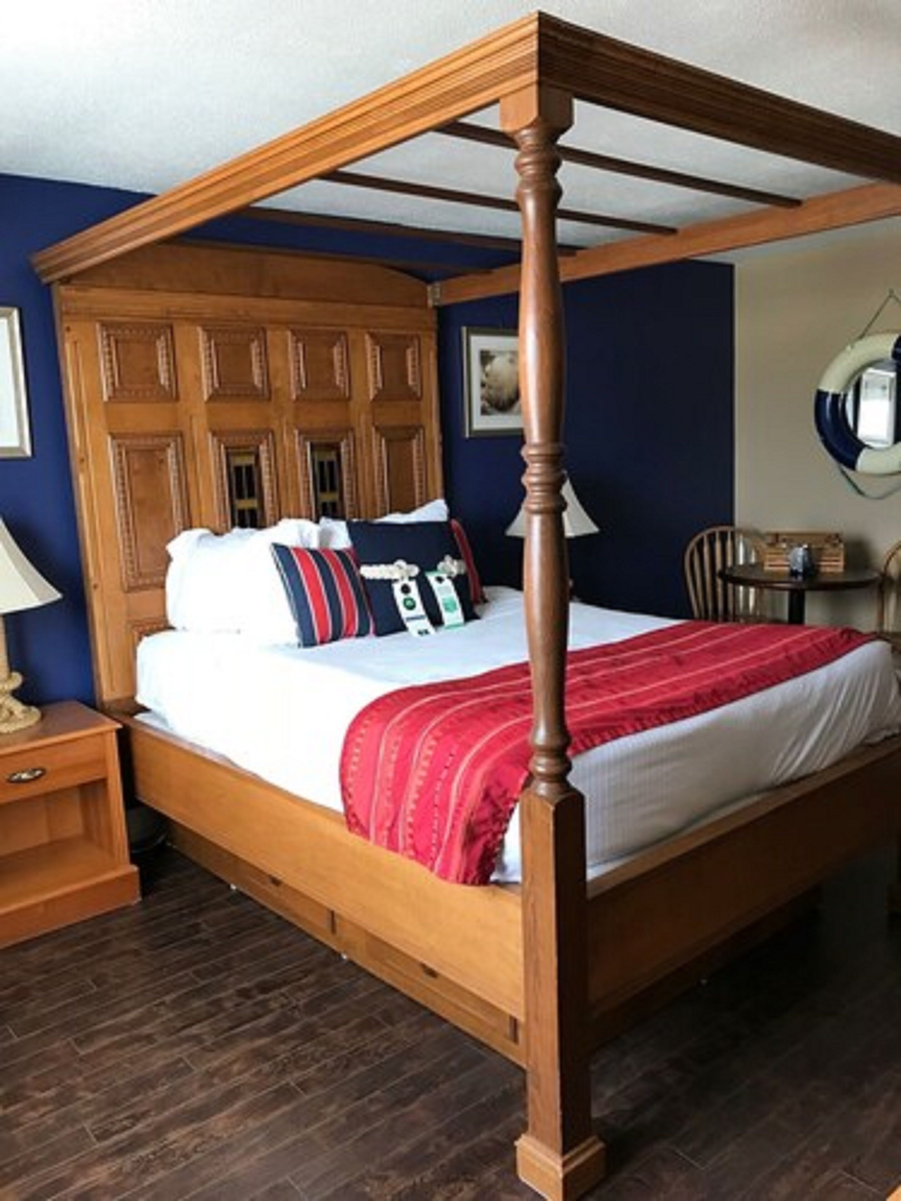 Uma cama com dossel, cabeceira de madeira, mesa de cabeceira e uma cadeira.