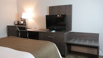 Quarto de hotel com cama, escrivaninha, cadeira, televisão e luminária.