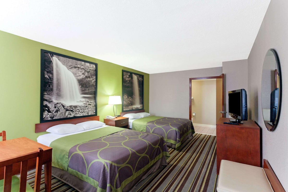 Quarto de hotel com duas camas, uma escrivaninha, uma cadeira, televisão e obras de arte nas paredes.