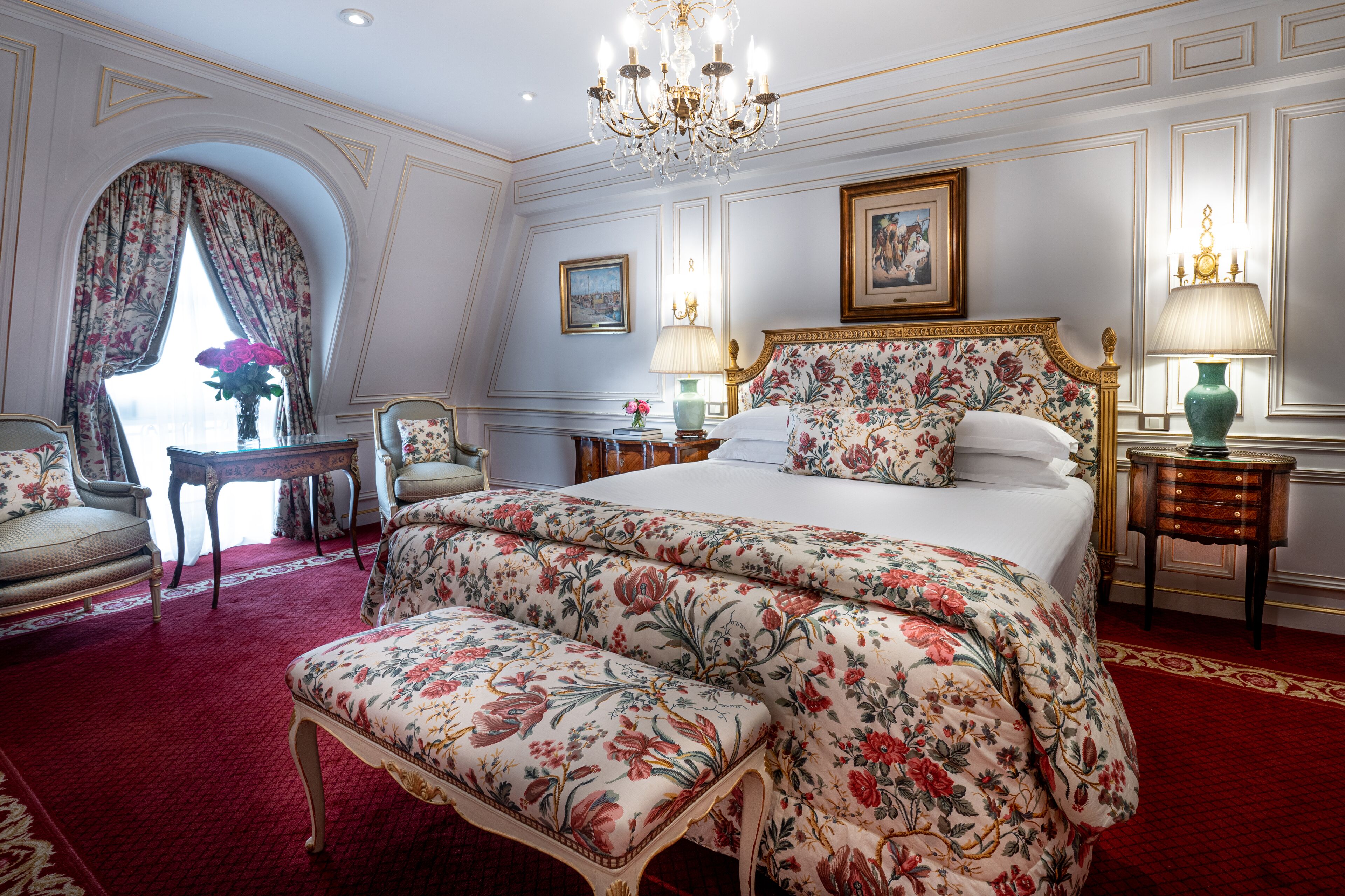 Um quarto luxuoso com espalha cama floral, um lustre e um tapete vermelho.
