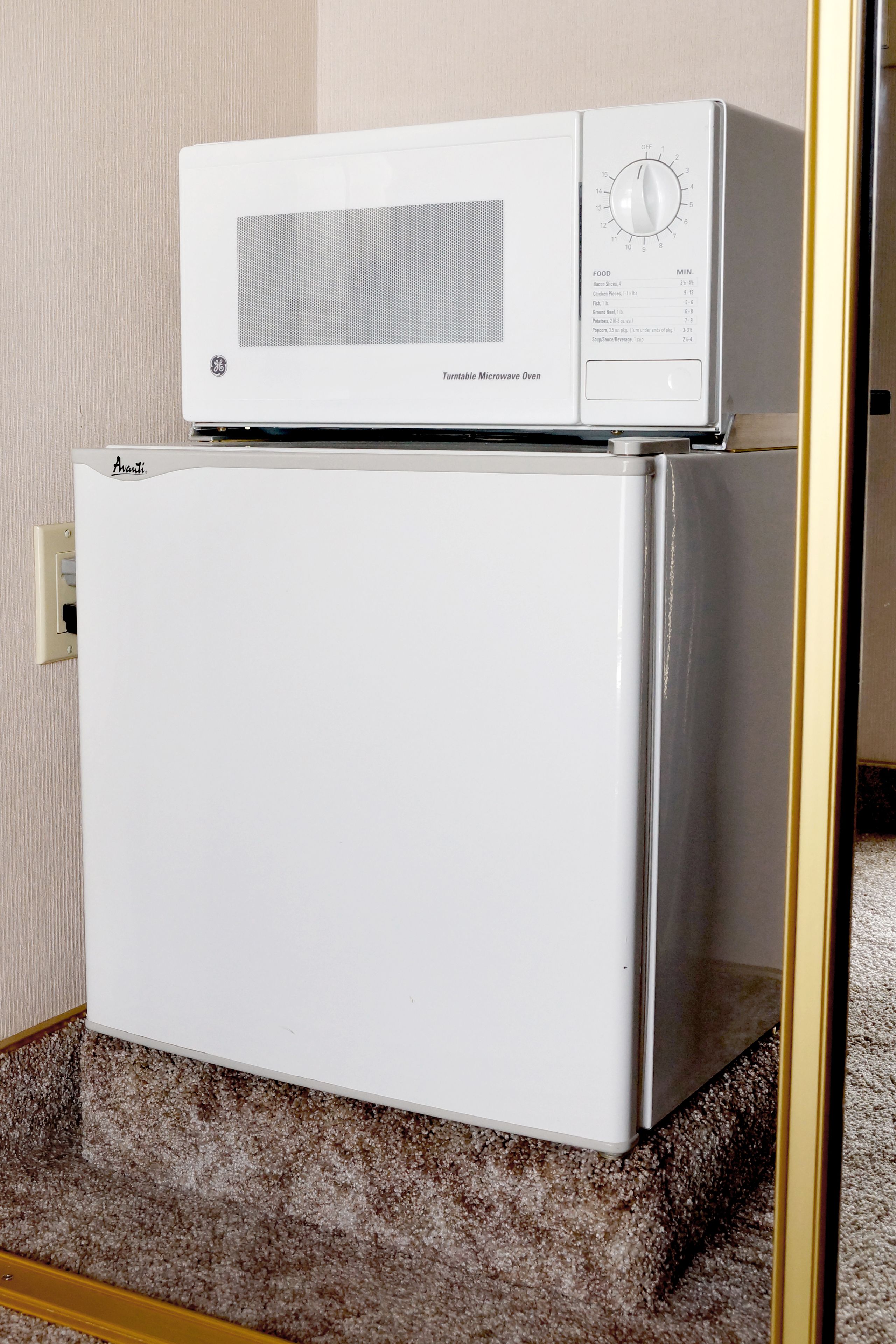 Uma geladeira compacta com micro-ondas embutido, posicionada sobre uma bancada de granito.