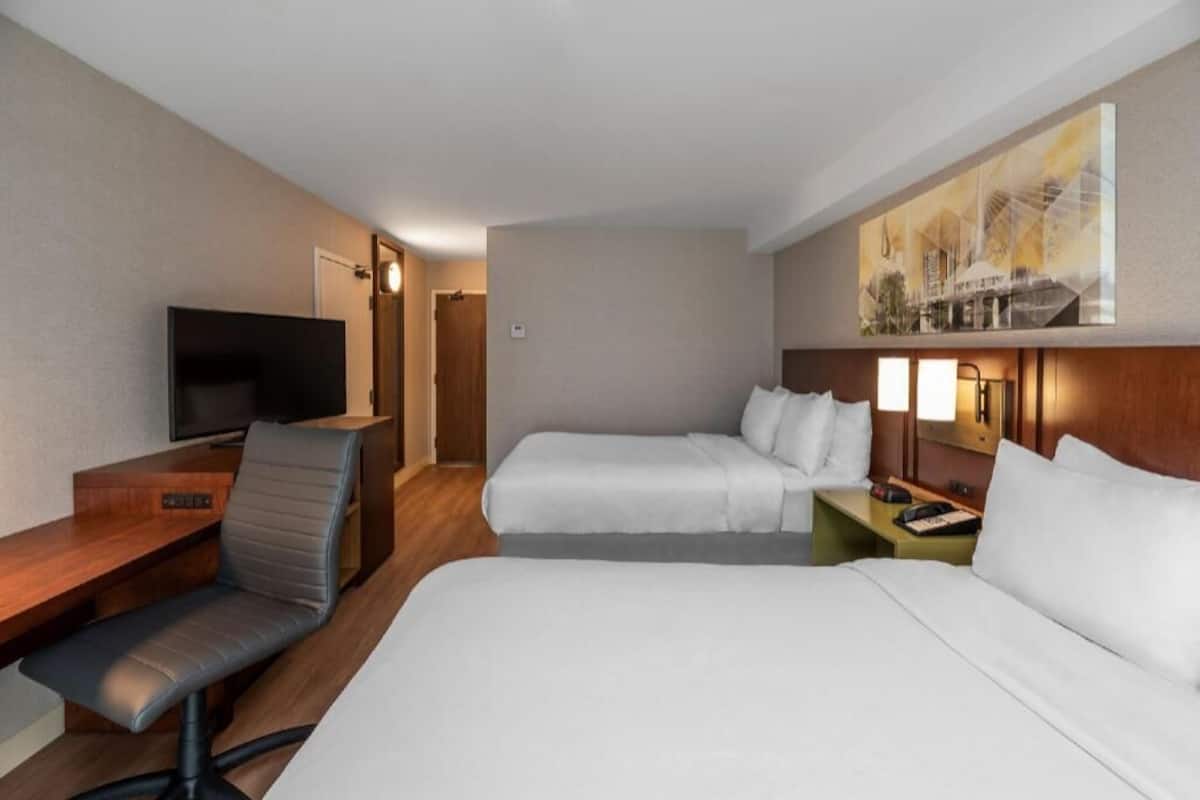 Quarto de hotel com escrivaninha, duas camas, televisão e um quadro na parede.