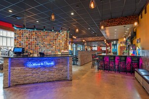 Interior de restaurante com parede azulejada, letreiro de neon e área de bar.