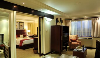 Quarto de hotel com cama, escrivaninha, cadeira, televisão e janela com cortinas.