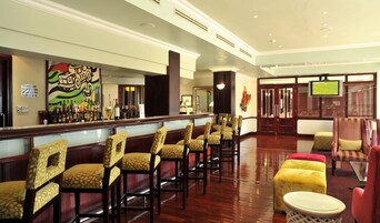 Uma área de bar com vários banquetas, um balcão com garrafas e uma tela de televisão.