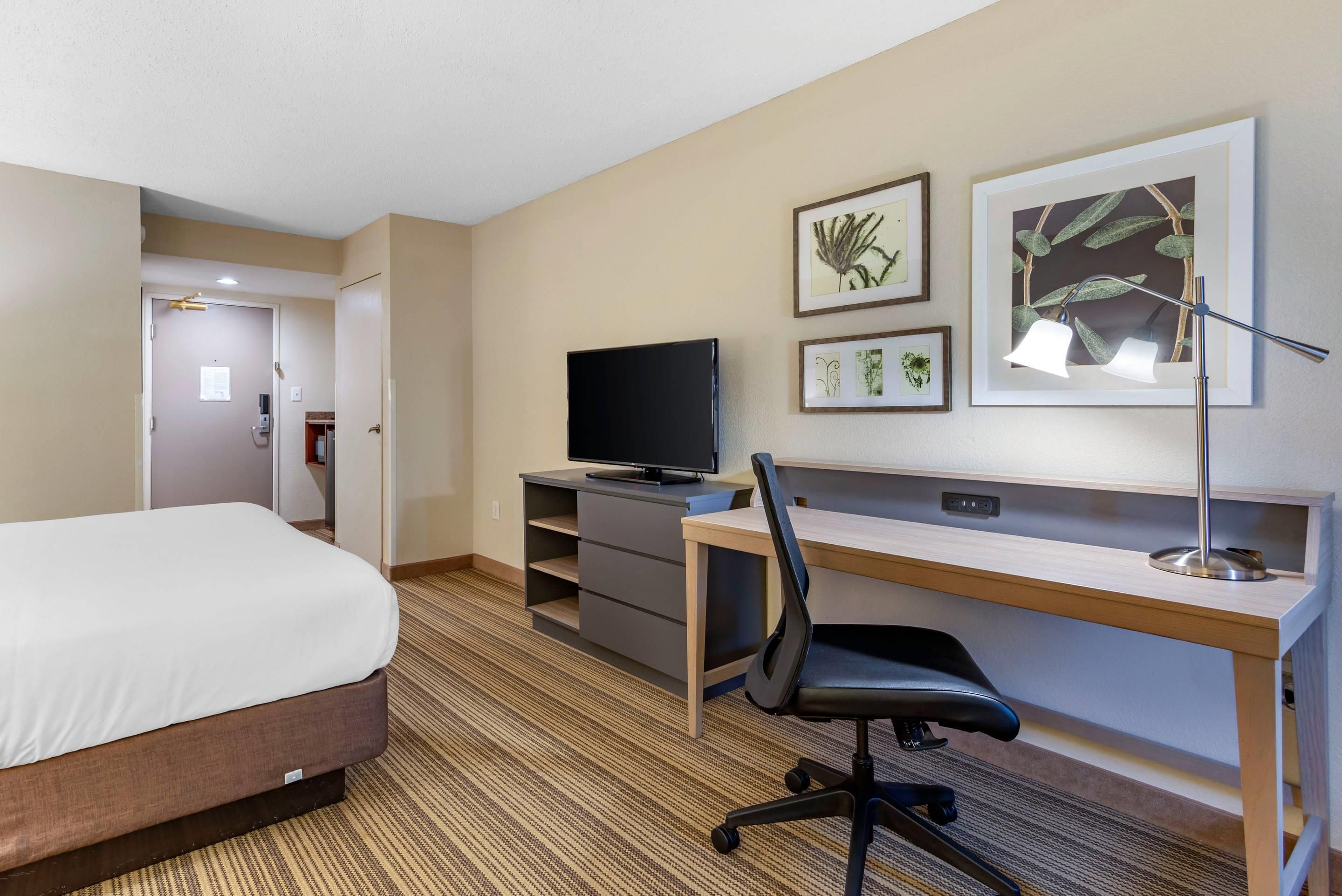 Quarto de hotel com cama, escrivaninha com computador, cadeira e televisão.