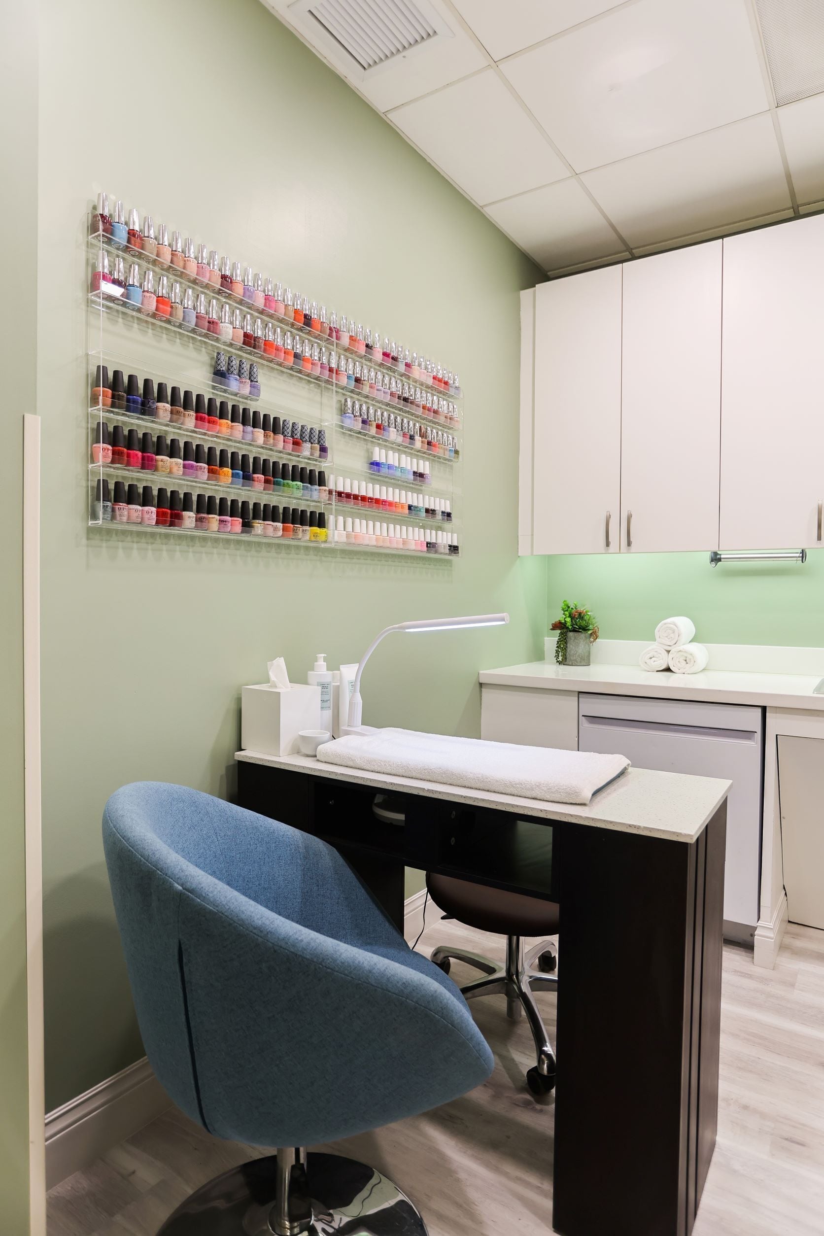 Um salão moderno com uma cadeira azul, um balcão com espelho e prateleiras com esmaltes.