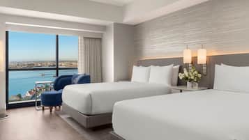 Quarto de hotel com duas camas, um sofá e vista para o mar e para a cidade.
