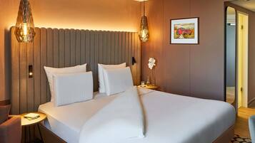 Quarto de hotel com uma cama grande, duas luminárias pendentes, uma mesinha com um livro e um quadro na parede.