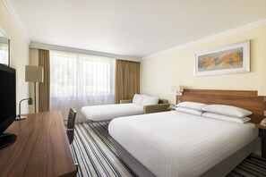 Quarto de hotel com duas camas, uma escrivaninha, uma televisão e uma janela com cortinas.