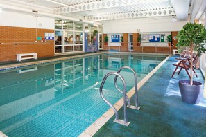 Piscina interna com água cristalina, escadas de metal e piso revestido com azulejos.