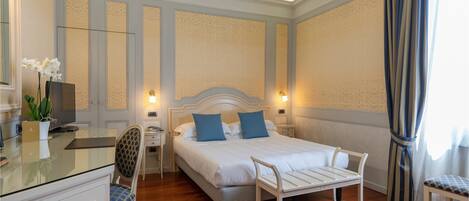 Quarto de hotel com uma cama grande, mesas de cabeceira, escrivaninha com cadeira, espelho e janela com cortinas.