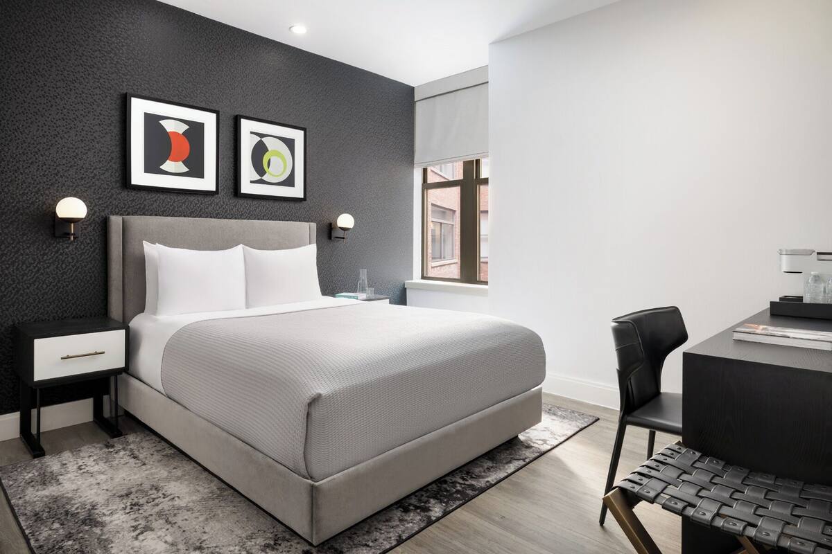 Quarto moderno com uma cama grande, mesas de cabeceira, escrivaninha e duas luminárias na parede.