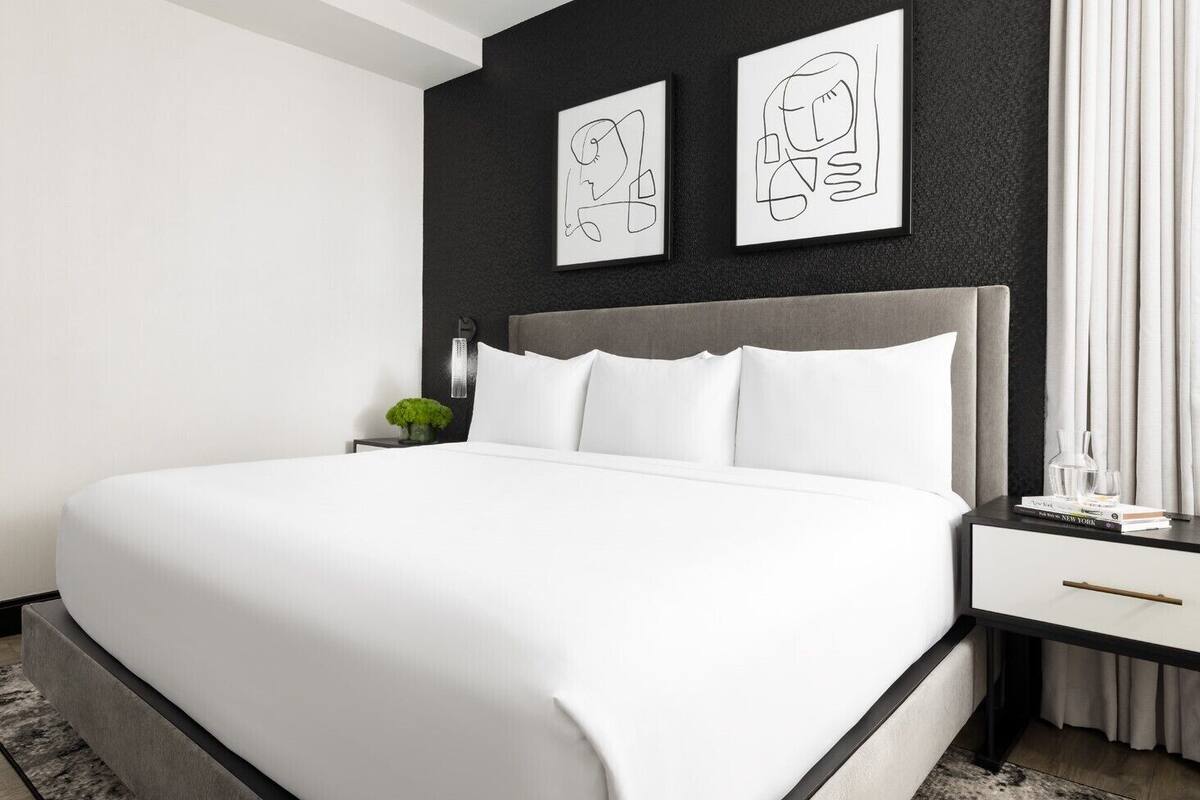 Quarto moderno com uma cama grande, cabeceira cinzenta e duas obras de arte emolduradas na parede.