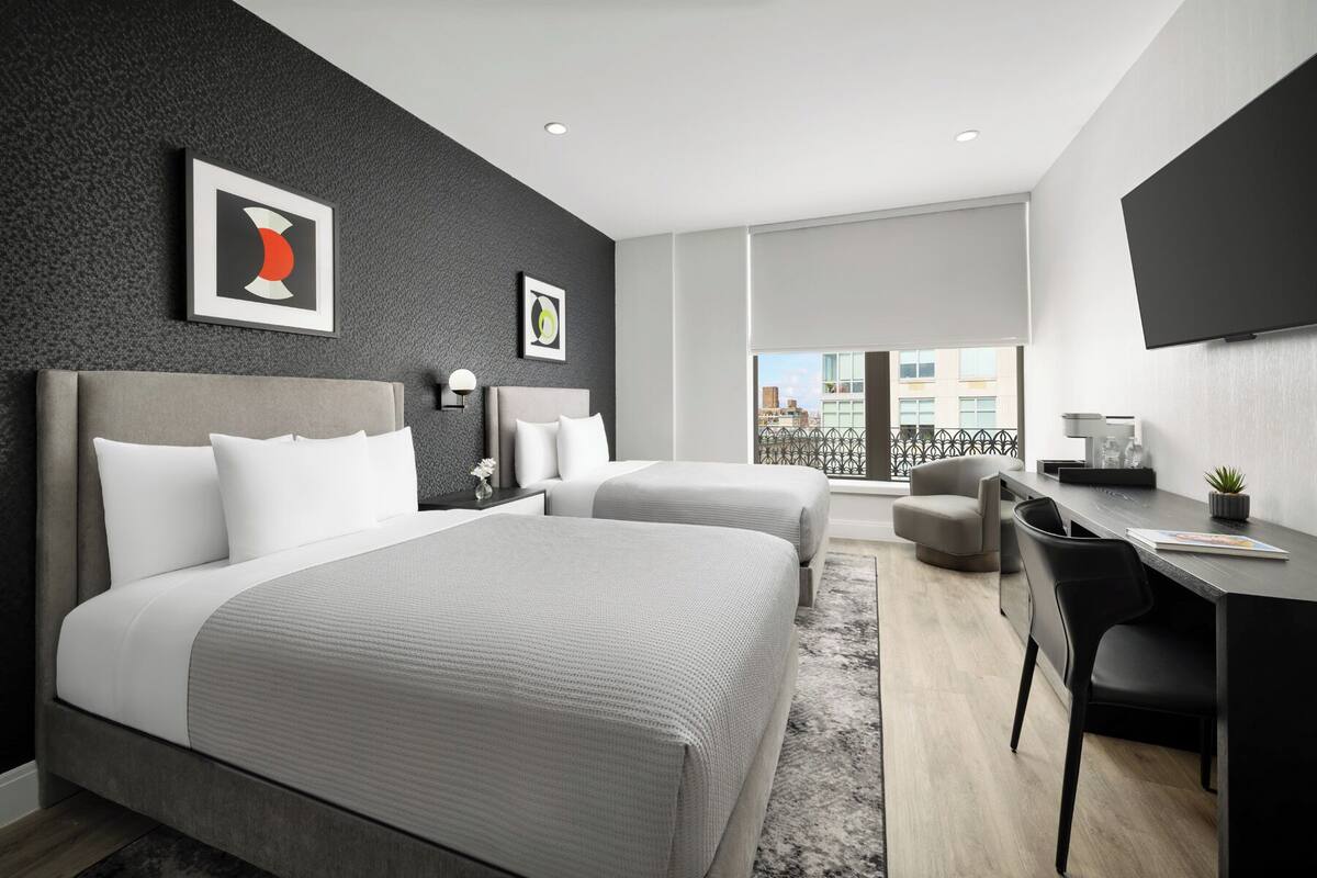Quarto de hotel moderno com duas camas, uma escrivaninha e uma televisão.