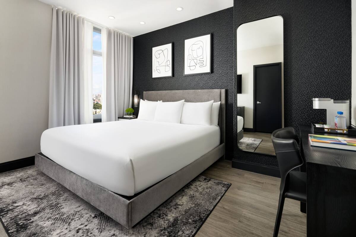 Quarto de hotel moderno com uma cama grande, uma escrivaninha e um espelho.