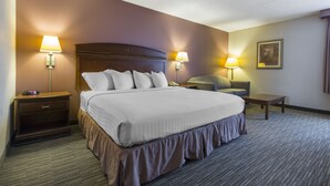 Quarto de hotel com uma cama grande, duas mesas de cabeceira com luminárias, uma mesinha e uma cadeira.
