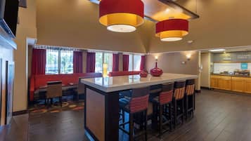 Um hall de hotel moderno com bar central, espaços para sentar e cozinha visível.