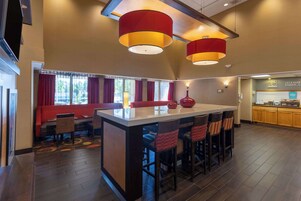 Um hall de hotel moderno com bar central, espaços para sentar e cozinha visível.