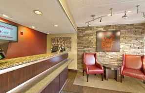 Área de recepção do Red Roof Inn, com painel digital, parede de pedra e assentos de couro.