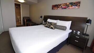 Quarto de hotel com uma cama grande, uma mesinha de cabeceira, uma cadeira e um quadro na parede.