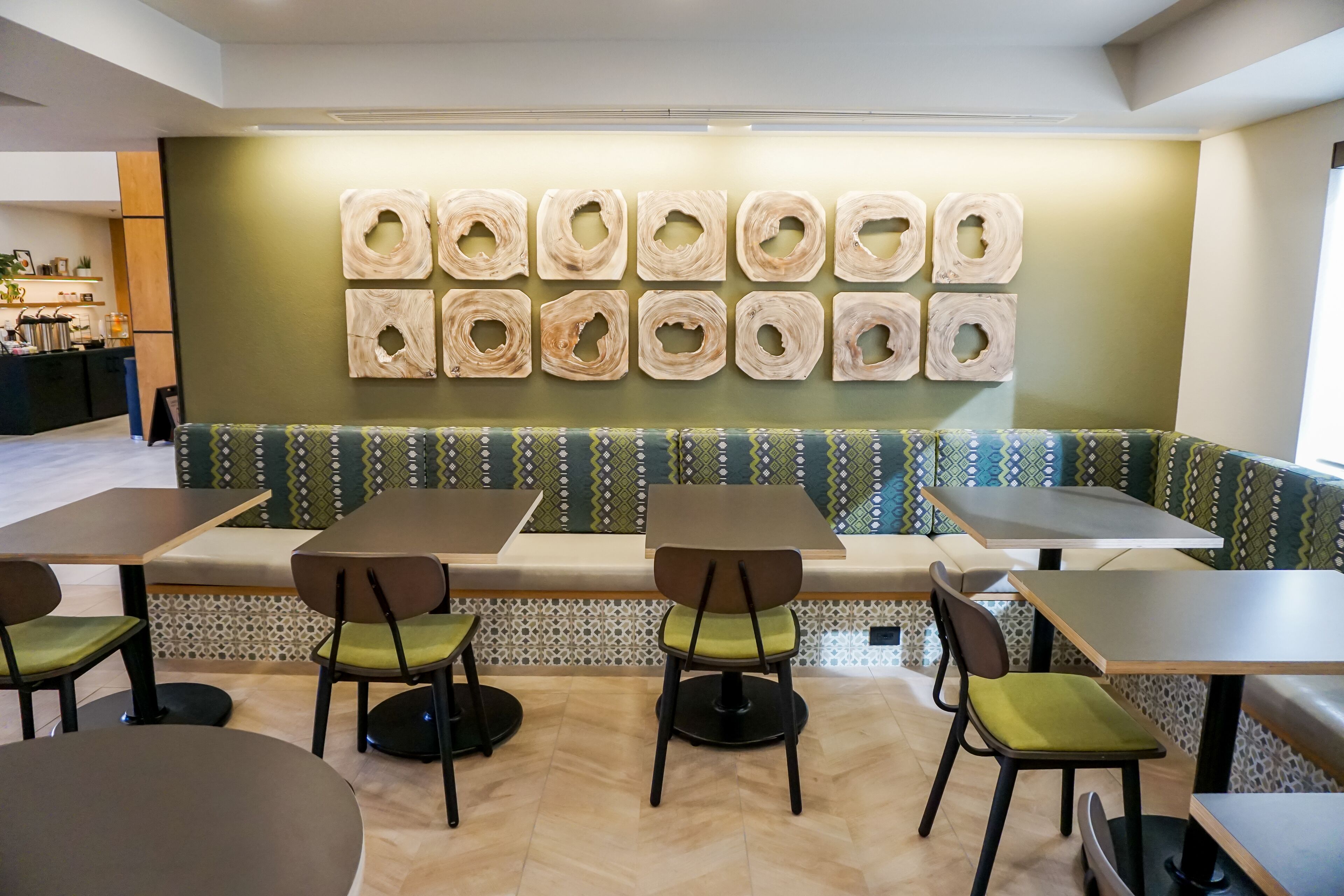 Restaurante com um banco de padrão verde, várias mesas e cadeiras com almofadas verdes.