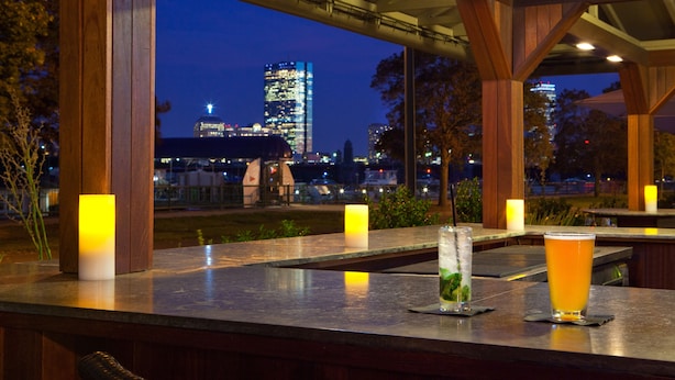 Um bar com duas bebidas, uma vela e vista para a cidade ao entardecer.