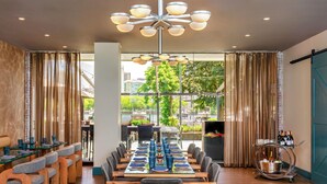 Uma sala de jantar com uma mesa longa posta para uma refeição, um candelabro e vista para o exterior.