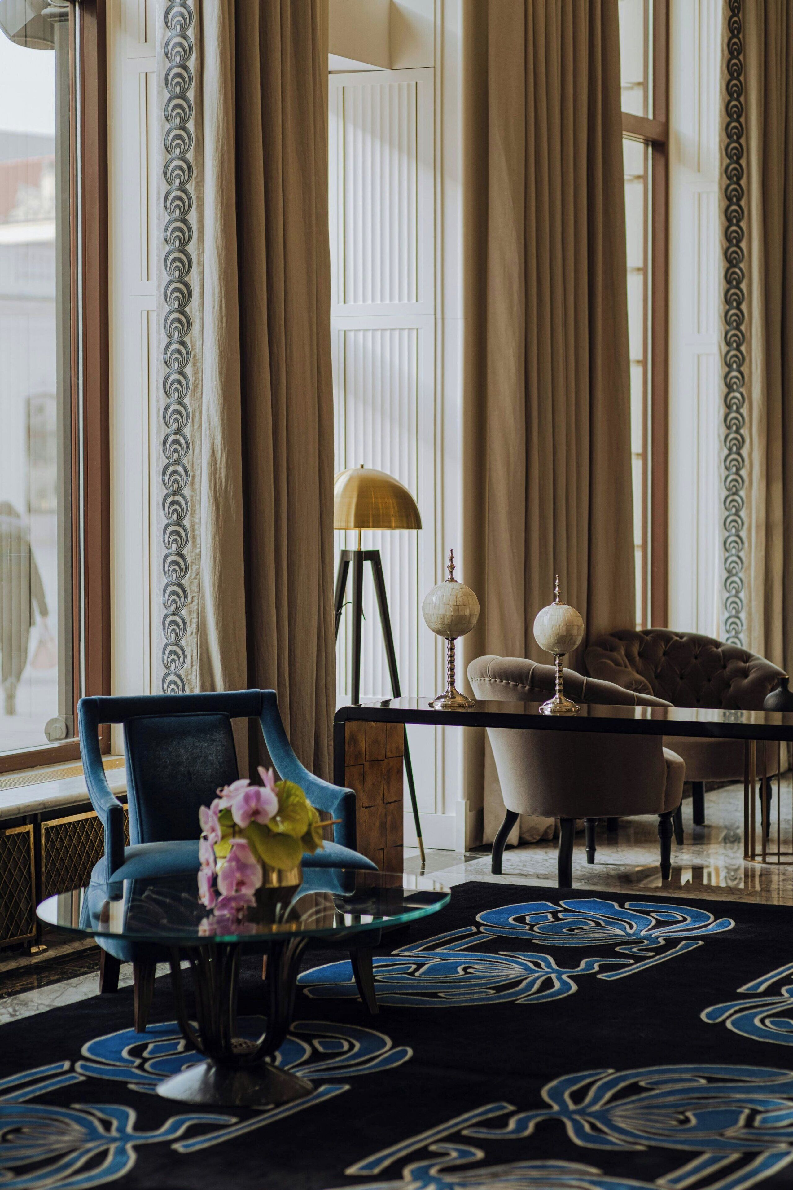 Um quarto com uma poltrona azul, uma mesa de centro de vidro com um vaso de flores, um sofá e um abajur.